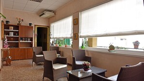 Quarto com mobiliário de vime, piso de azulejos e grandes janelas com persianas brancas.