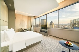 Quarto de hotel com cama grande, televisão, escrivaninha e vista para a paisagem urbana.