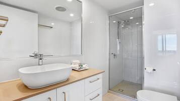 Uma casa de banho moderna com uma grande pia branca, um chuveiro com divisória de vidro e uma sanita.