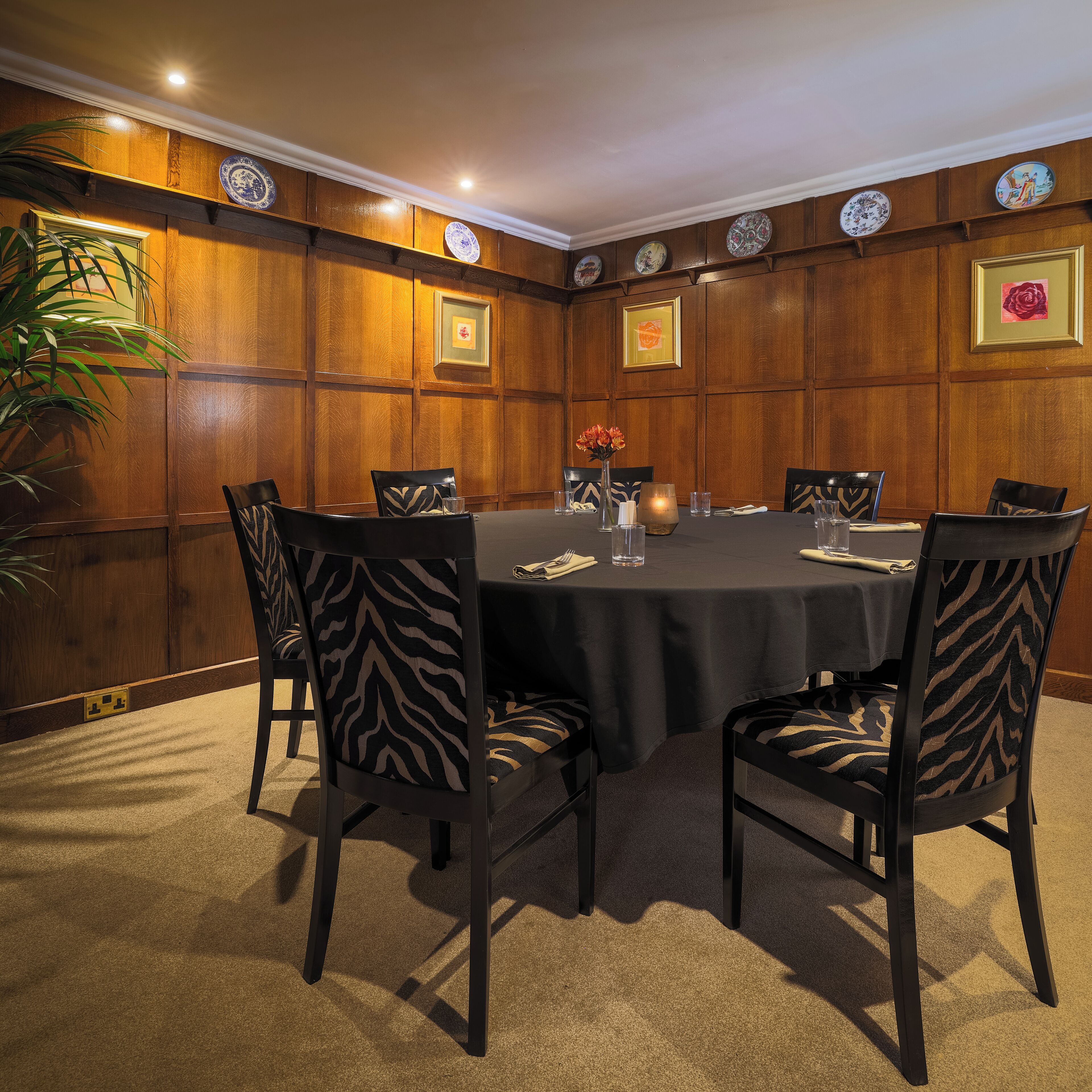 Uma sala de conferências com uma mesa redonda, cadeiras com padrão de zebra e painéis de madeira nas paredes.