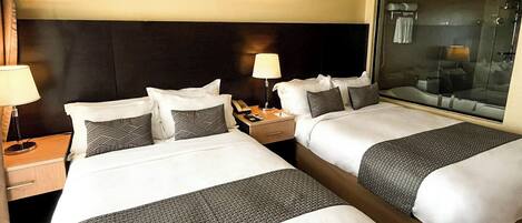 Quarto de hotel com duas camas, um espelho grande, mesa de cabeceira com abajur e ar condicionado fixado na parede.