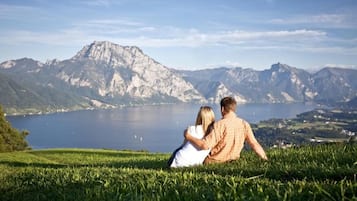 Um casal sentado numa colina gramada com vista para um lago e montanhas.