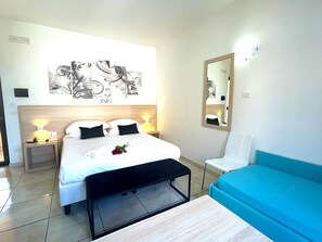 Quarto de hotel com uma cama, abajures, um espelho, um sofá azul e uma parede com arte abstrata.