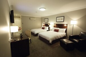 Quarto de hotel com duas camas, uma escrivaninha, uma cadeira, uma televisão e um abajur.