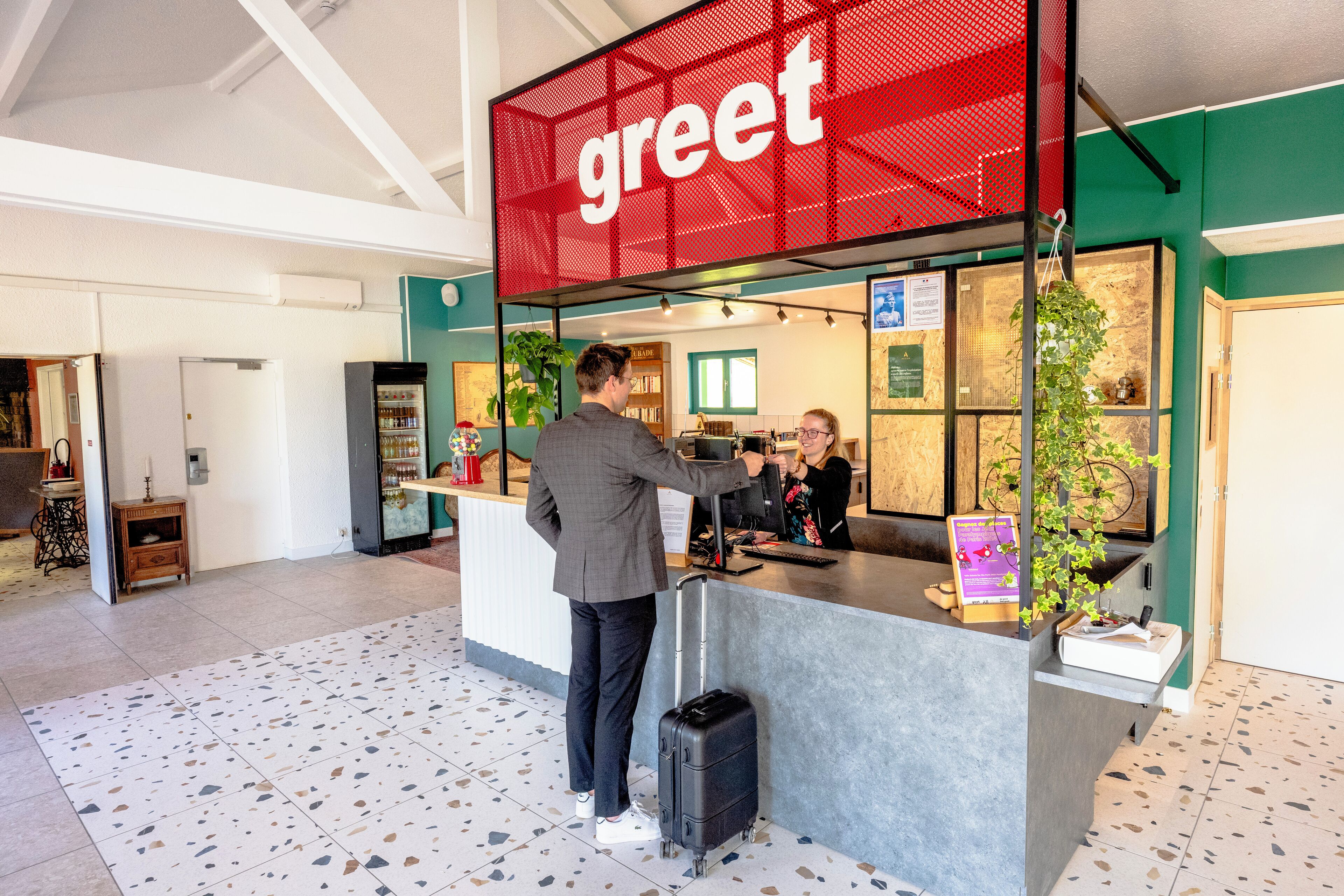 Uma área de recepção com um letreiro que diz 'greet', balcão, computador e planta.