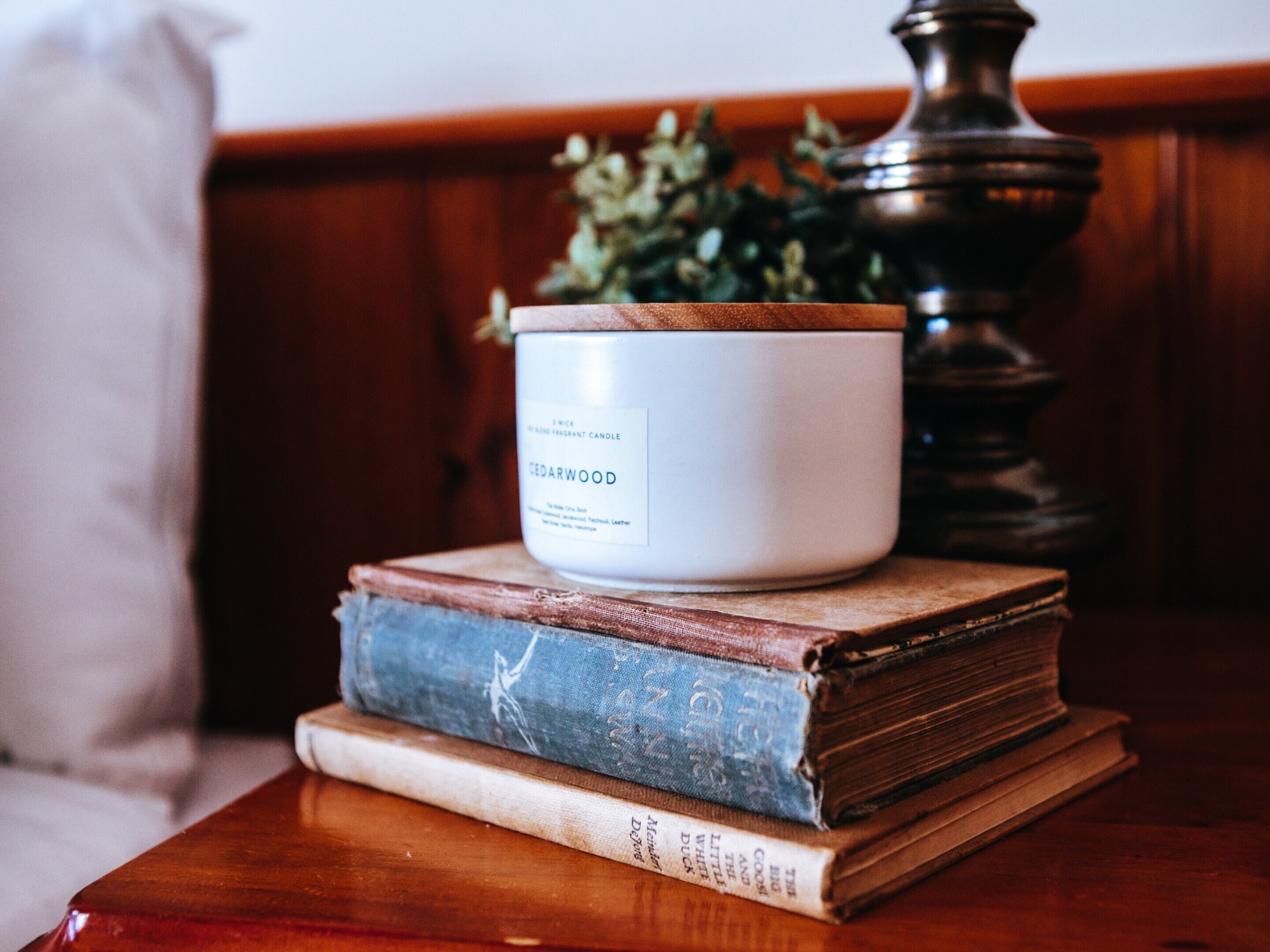 Uma vela branca com a etiqueta 'Cedarwood' sobre uma pilha de livros.