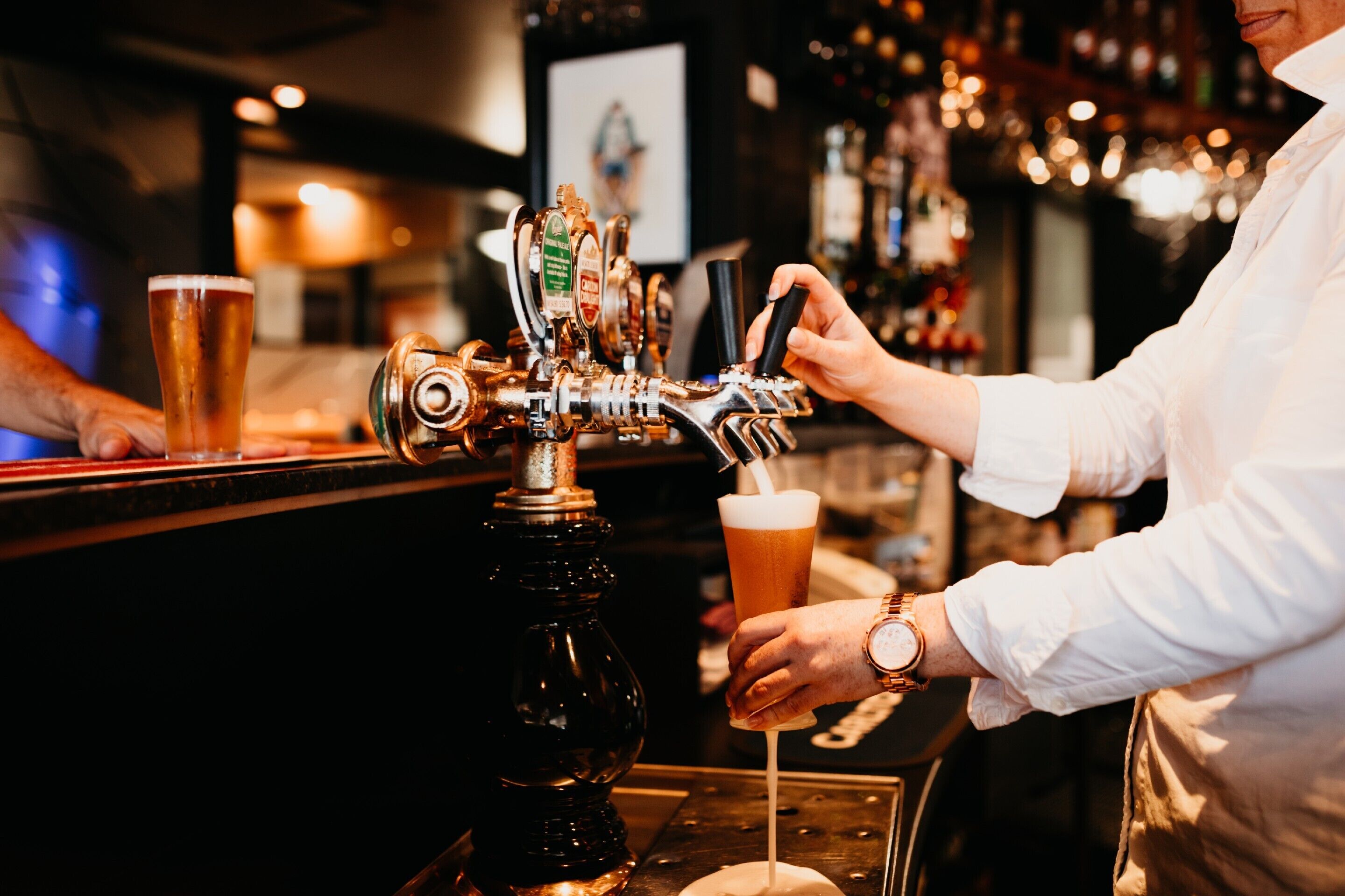 Um bartender servindo cerveja em um copo no balcão.