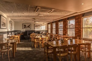 Um restaurante com mesas e cadeiras de madeira, paredes de tijolo e janelas amplas.