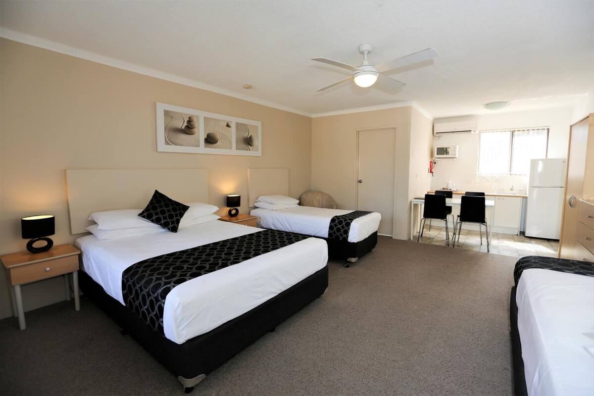 Quarto de hotel com duas camas, uma escrivaninha e uma cozinha compacta.