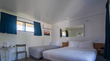 Quarto com duas camas de solteiro, uma mesinha com uma cadeira, um espelho e uma janela com cortinas.