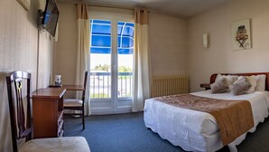 Quarto de hotel com cama, mesa de cabeceira, cadeira, escrivaninha e varanda com vista.