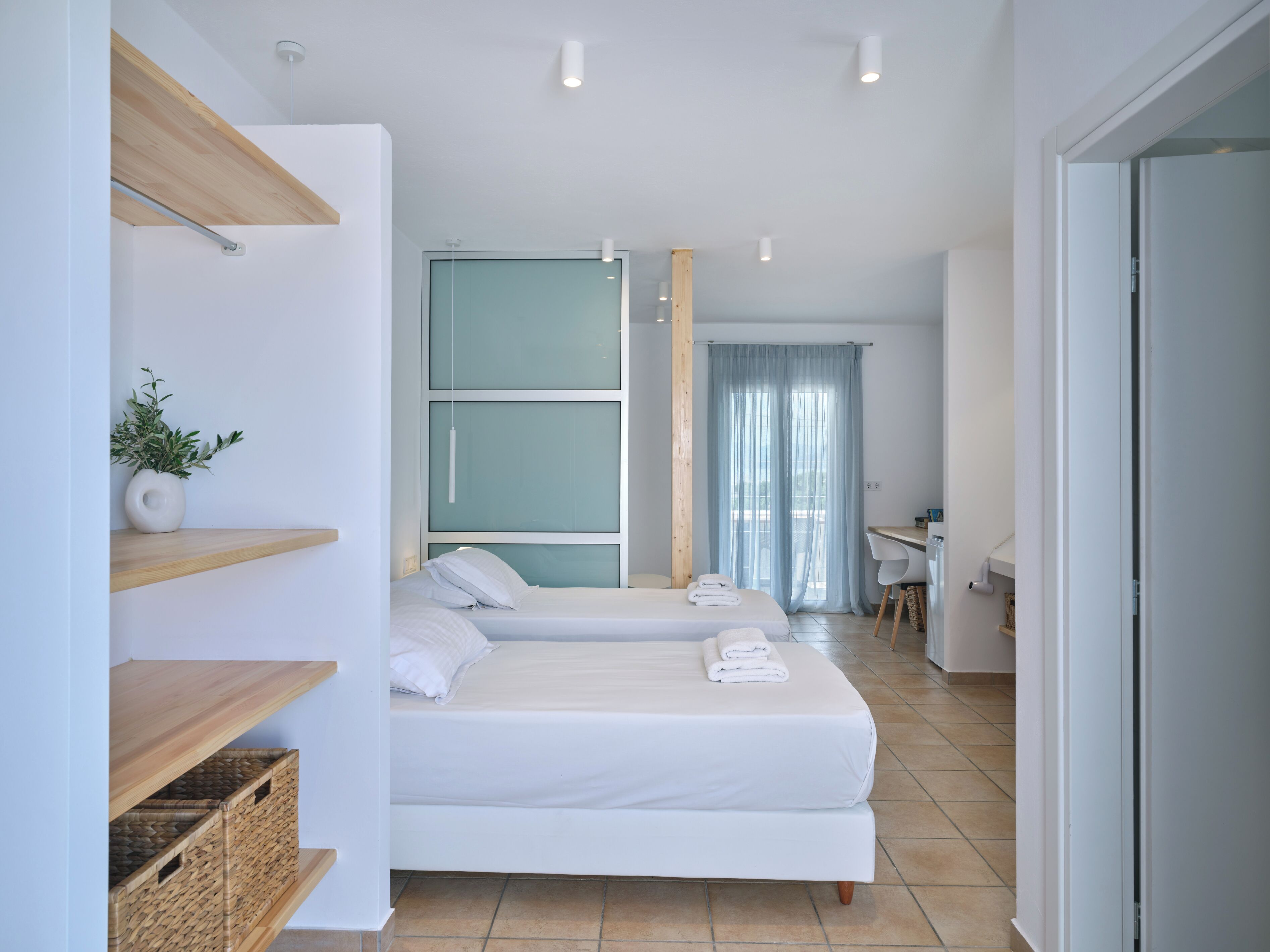 Quarto de hotel moderno com duas camas, uma mesa de trabalho e uma janela grande com cortinas.
