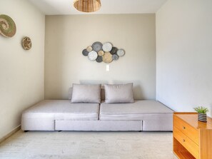 Quarto minimalista com sofá cinzento, mesa lateral de madeira e composição de pratos decorativos na parede.