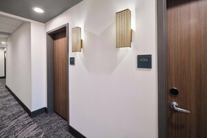 Corredor de hotel com piso carpeteado, duas portas com os números 432 e 433, e luminárias fixadas na parede.