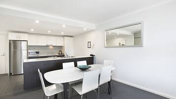 Uma cozinha moderna com armários brancos, forno embutido e sala de jantar com mesa e cadeiras brancas.