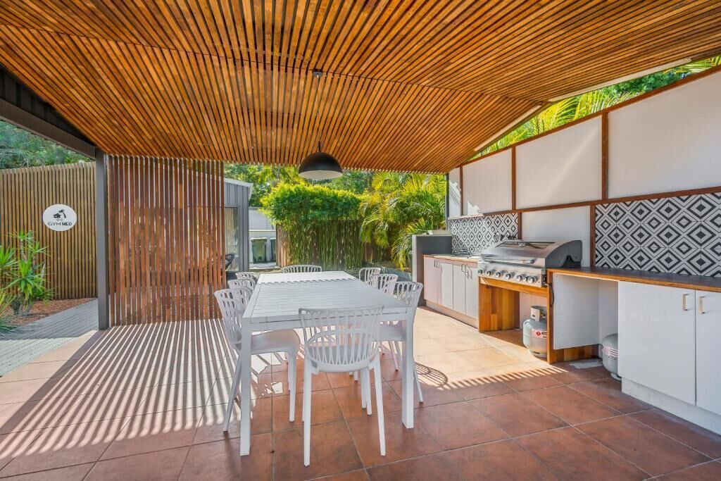 Uma área de refeições ao ar livre com mesa, cadeiras, estação de churrasco e painel decorativo.