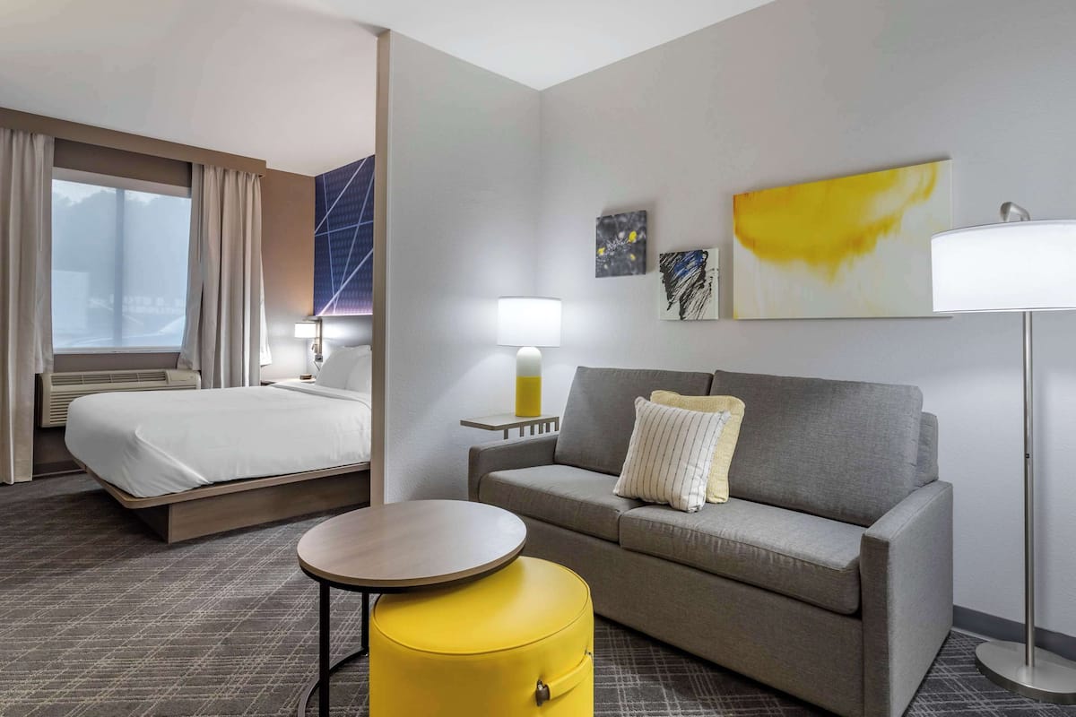 Quarto de hotel com cama, sofá, uma mesinha e abajur.