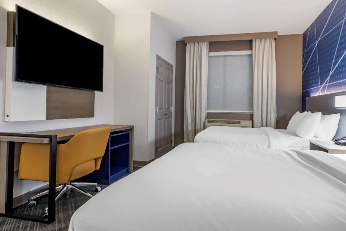 Quarto de hotel com uma cama, uma escrivaninha com cadeira, televisão e janela com cortinas.