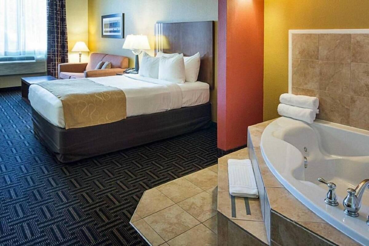 Quarto de hotel com cama, banheiro com banheira e janela com cortinas.