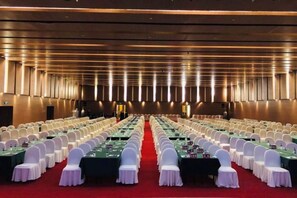 Sala de conferências com fileiras de mesas e cadeiras, equipada com microfones e projetores.