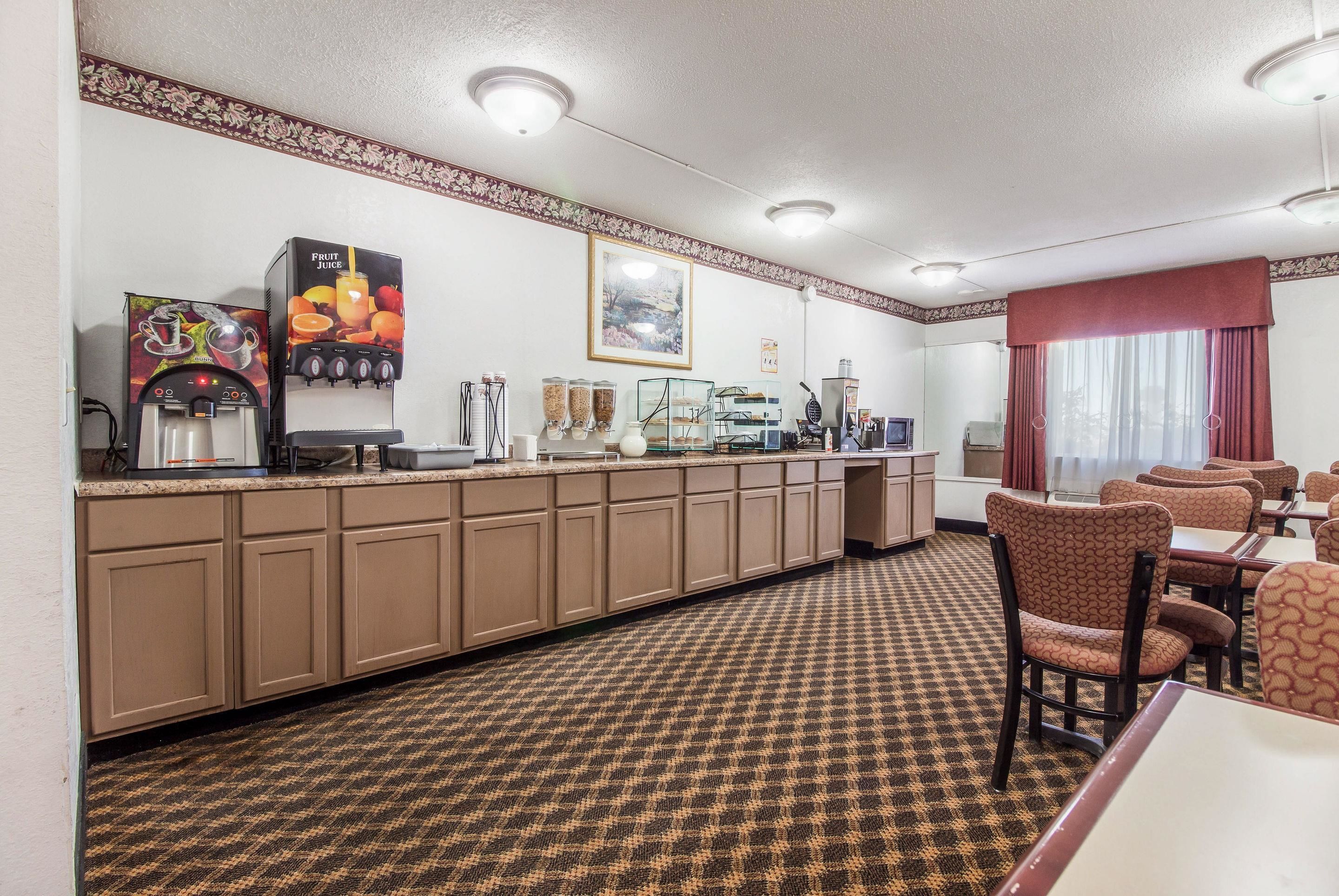 Quarto de hotel com cozinha compacta, máquina de café, dispensador de suco de fruta e carpete estampado.