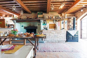 Uma cozinha rústica com lareira de tijolos, vigas de madeira e um espaço de jantar com mesa posta para dois.