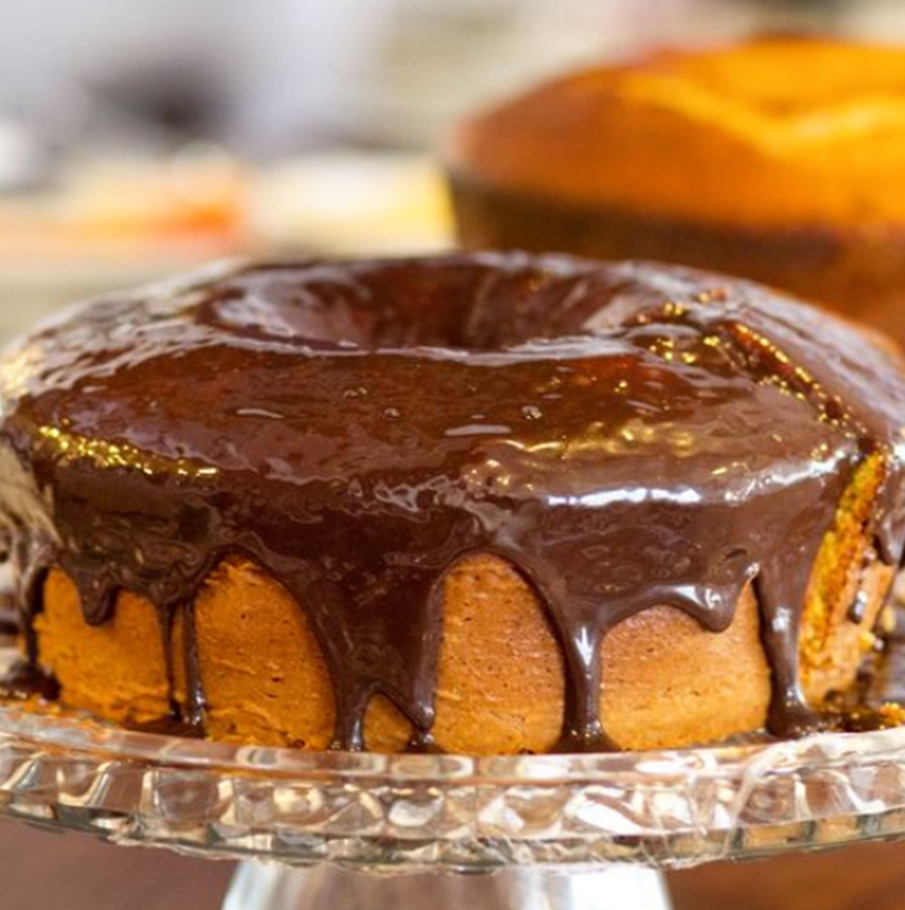 Um bolo com cobertura de chocolate sobre um suporte de vidro.