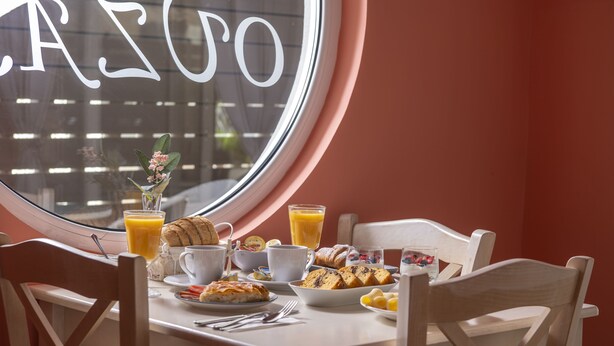 Uma mesa de café da manhã com diversos alimentos e bebidas, em frente a uma janela com vista para uma cerca.