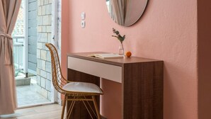 Quarto com parede rosa, espelho redondo, escrivaninha de madeira, cadeira de vime e janela com cortinas.