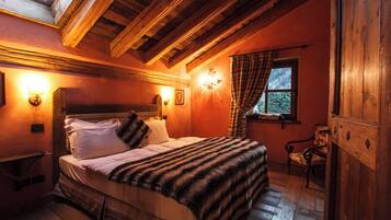 Quarto aconchegante com teto de madeira, uma cama com manta listrada, mesa de cabeceira, uma cadeira e uma janela com cortinas.