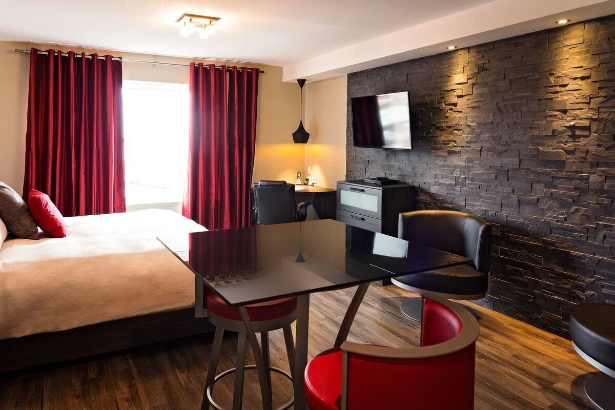 Quarto de hotel moderno com cama, escrivaninha, cadeira, televisão e parede de pedra.