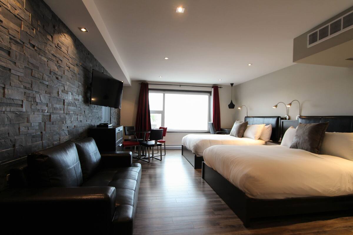 Quarto de hotel moderno com cama grande, sofá, escrivaninha e televisão fixada na parede.