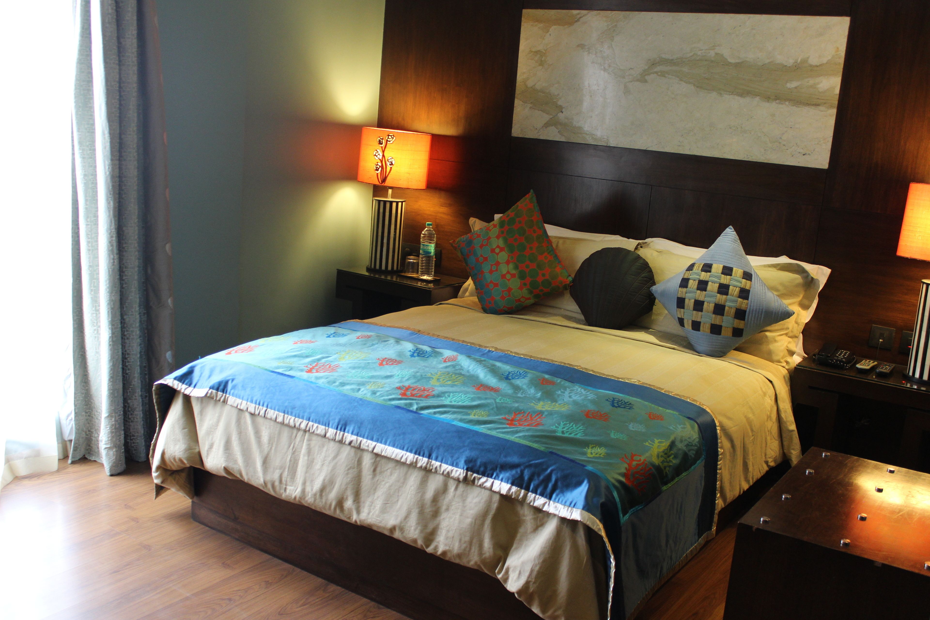 Cama bem arrumada com colcha floral, duas luminárias de cabeceira e uma mesinha de noite com telefone e garrafa.