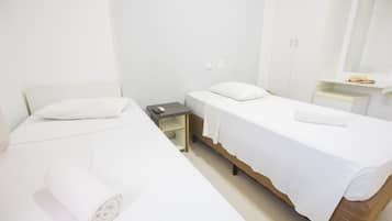 Quarto de hotel com duas camas de solteiro, uma mesinha, um criado-mudo e um espelho.