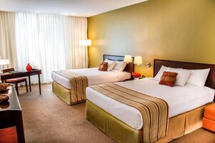 Quarto de hotel com duas camas, uma escrivaninha e uma cadeira.