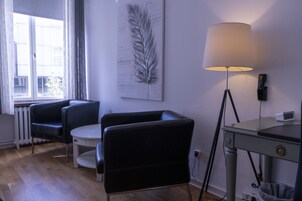 Quarto moderno com sofá de couro preto, uma pequena mesa redonda, luminária de pé e radiador.