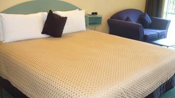Quarto de hotel com cama grande, mesa de cabeceira, cadeira e janela com cortinas.