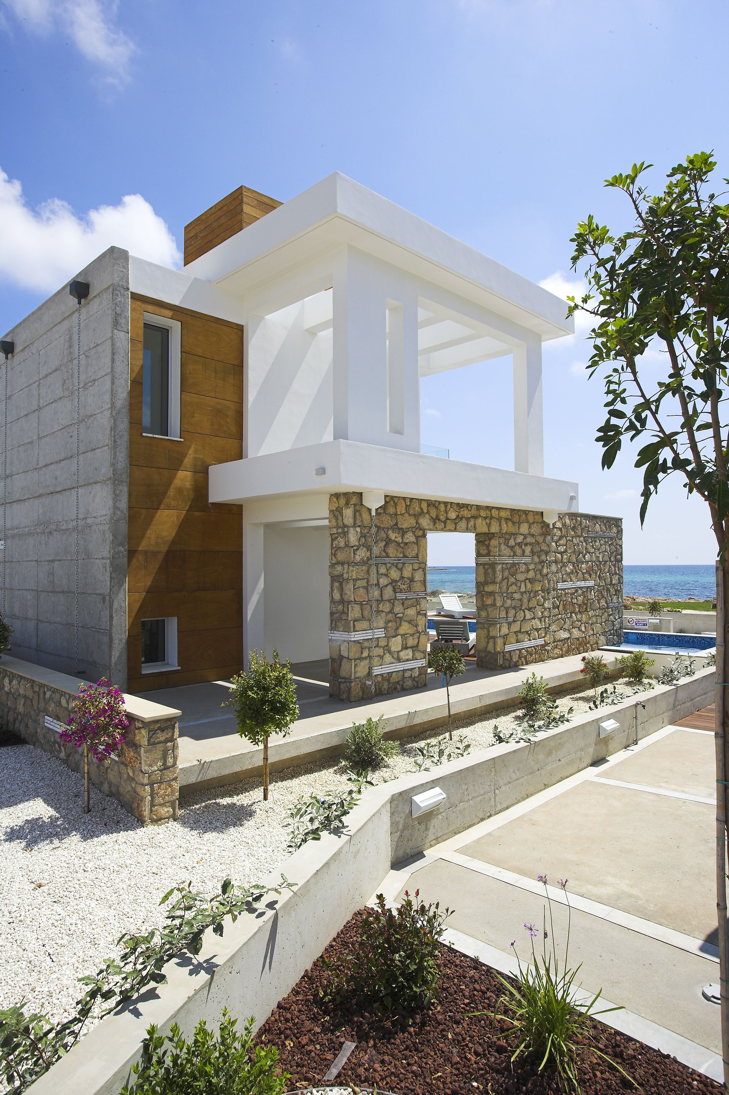 Uma casa moderna com fachada de pedra, parte em madeira e vista para o mar.