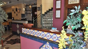 Um saguão de hotel com balcão de recepção, escadaria e parede decorativa.