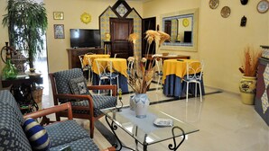 Sala de estar com sofá, cadeiras, mesa de centro, televisão e área de jantar com toalhas de mesa amarelas.