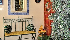 Um banco com almofadas decorativas, um espelho com moldura azul e um vaso grande com planta.