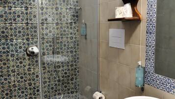 Casa de banho com chuveiro, sanita, lavatório e azulejos decorativos.