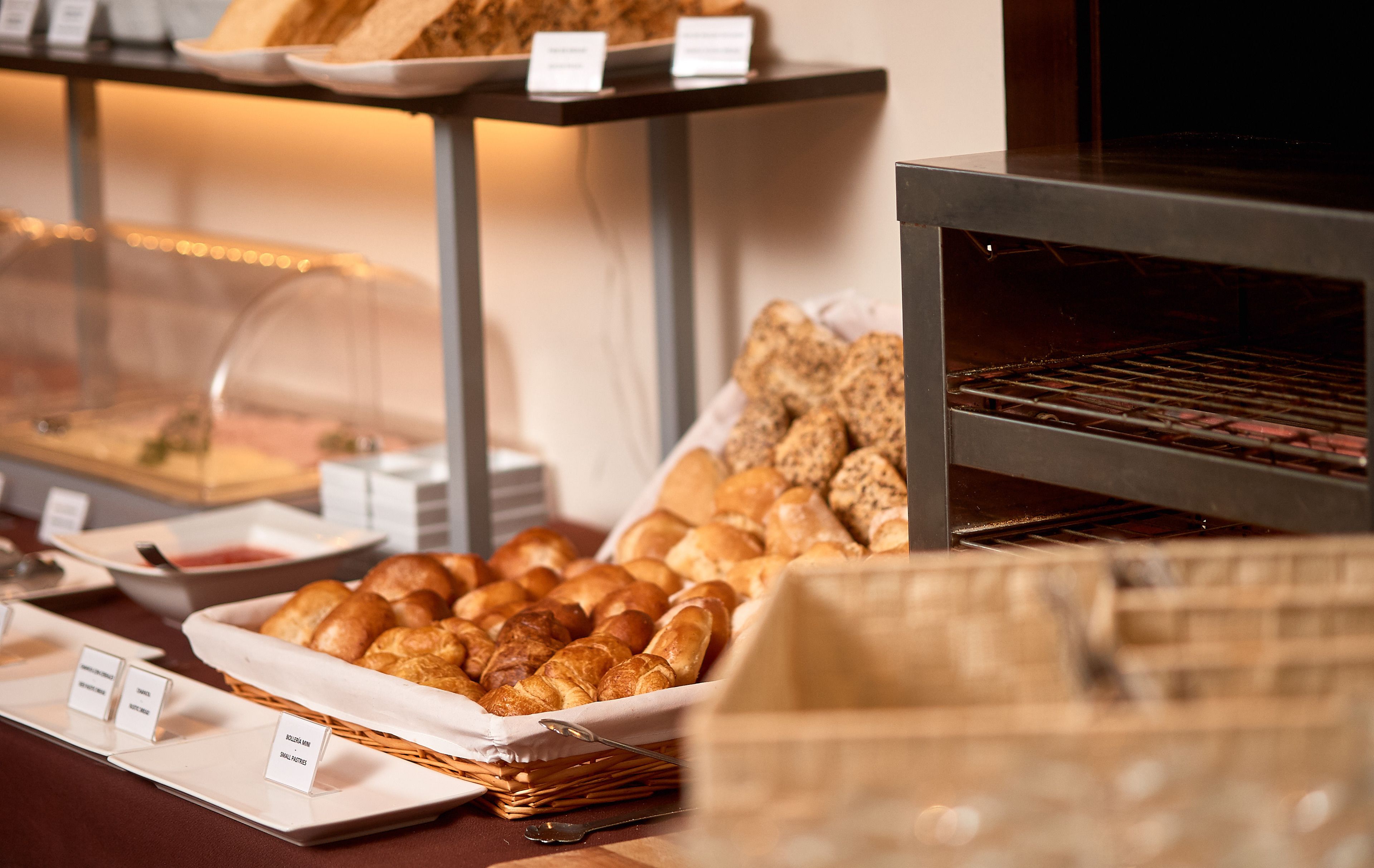 Buffet com diversos pães e doces, dispostos em bandejas e cestas.