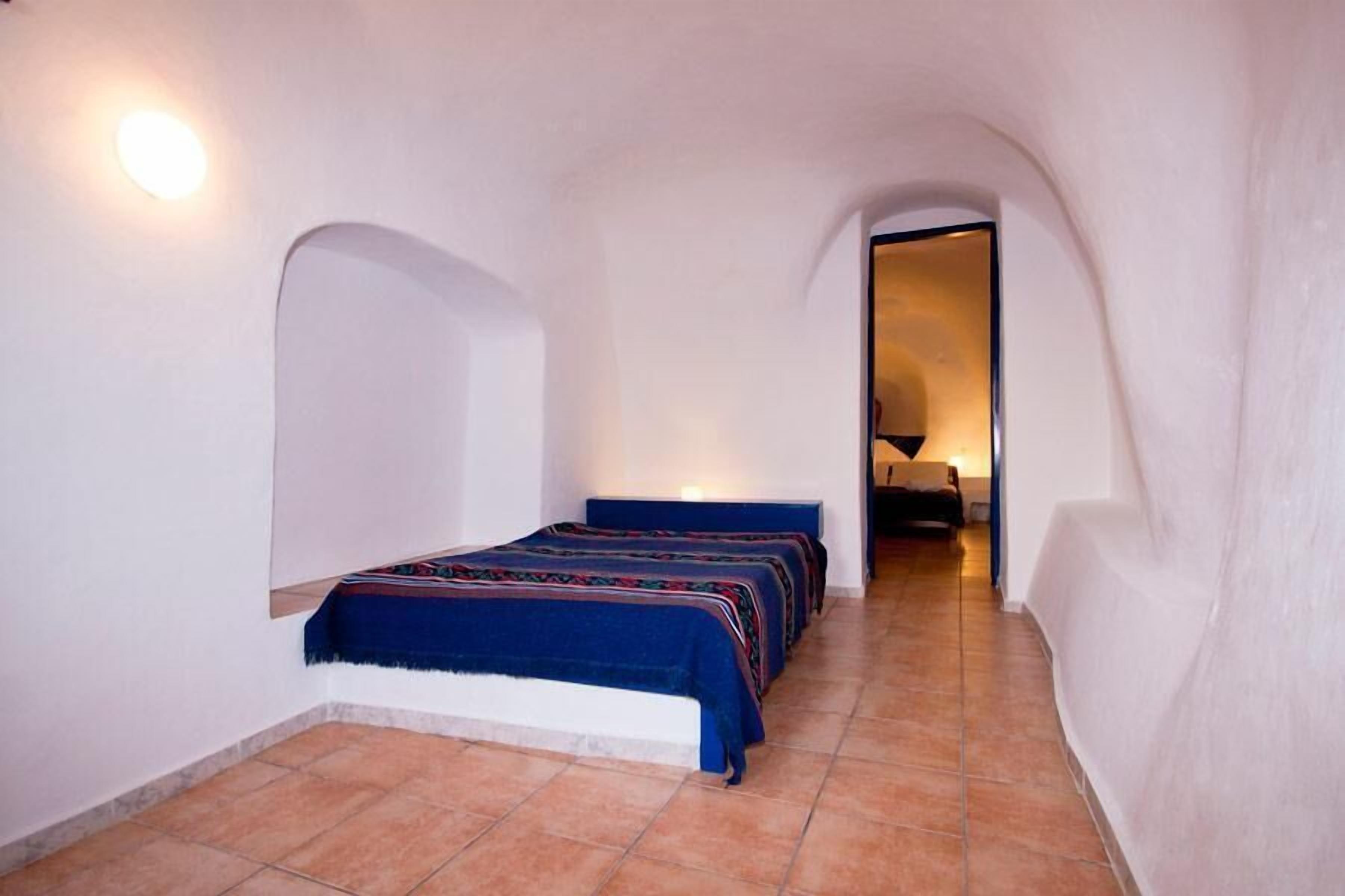 Quarto com cama, mesa de cabeceira e luminária na parede.