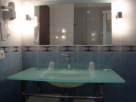 Uma casa de banho com lavatório de vidro, dois espelhos, secador de cabelo e um porta-toalhas.
