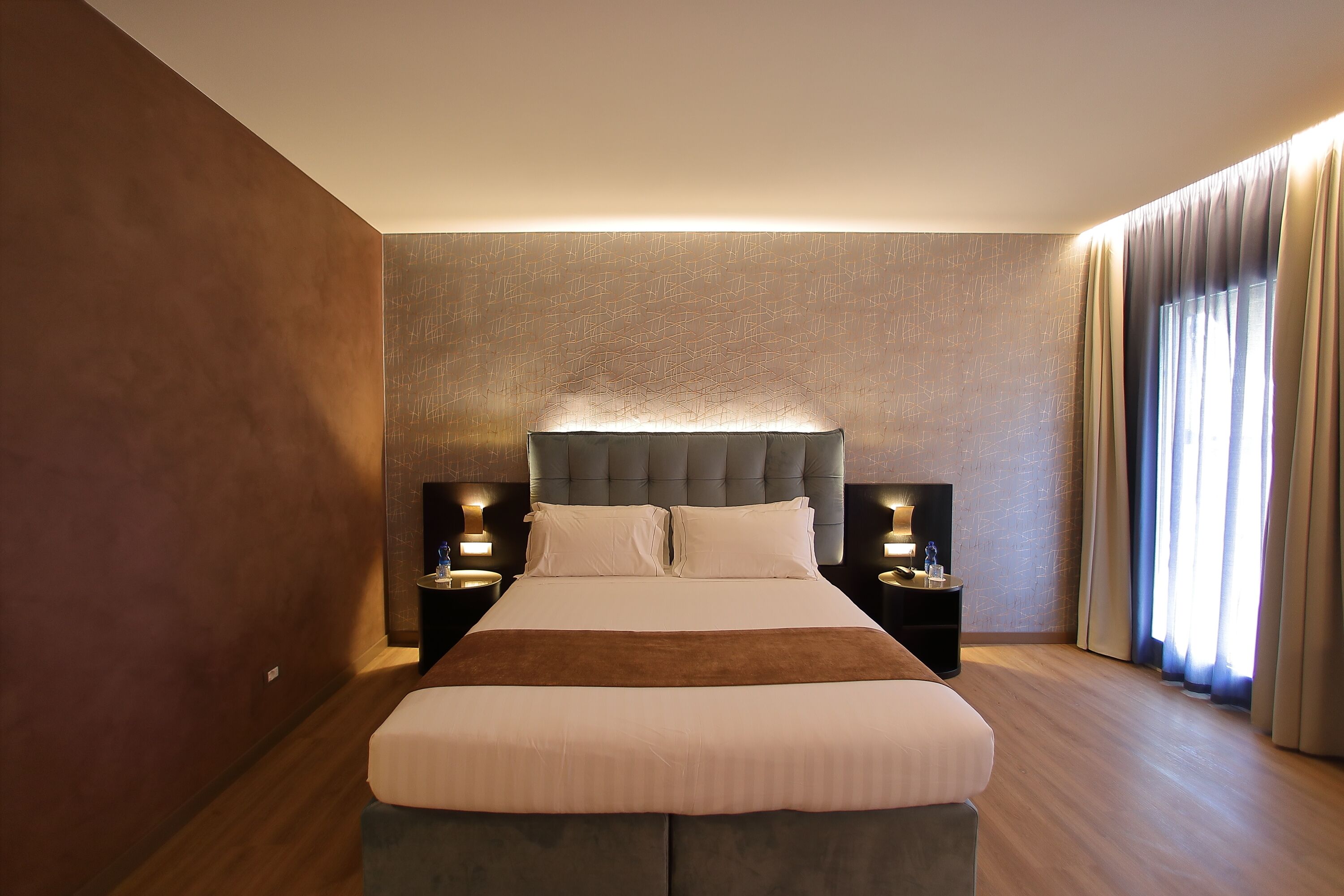 Quarto de hotel moderno com uma cama grande, duas mesas de cabeceira e cabeceira com iluminação integrada.