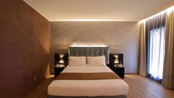 Quarto de hotel moderno com uma cama grande, duas mesas de cabeceira e cabeceira com iluminação integrada.