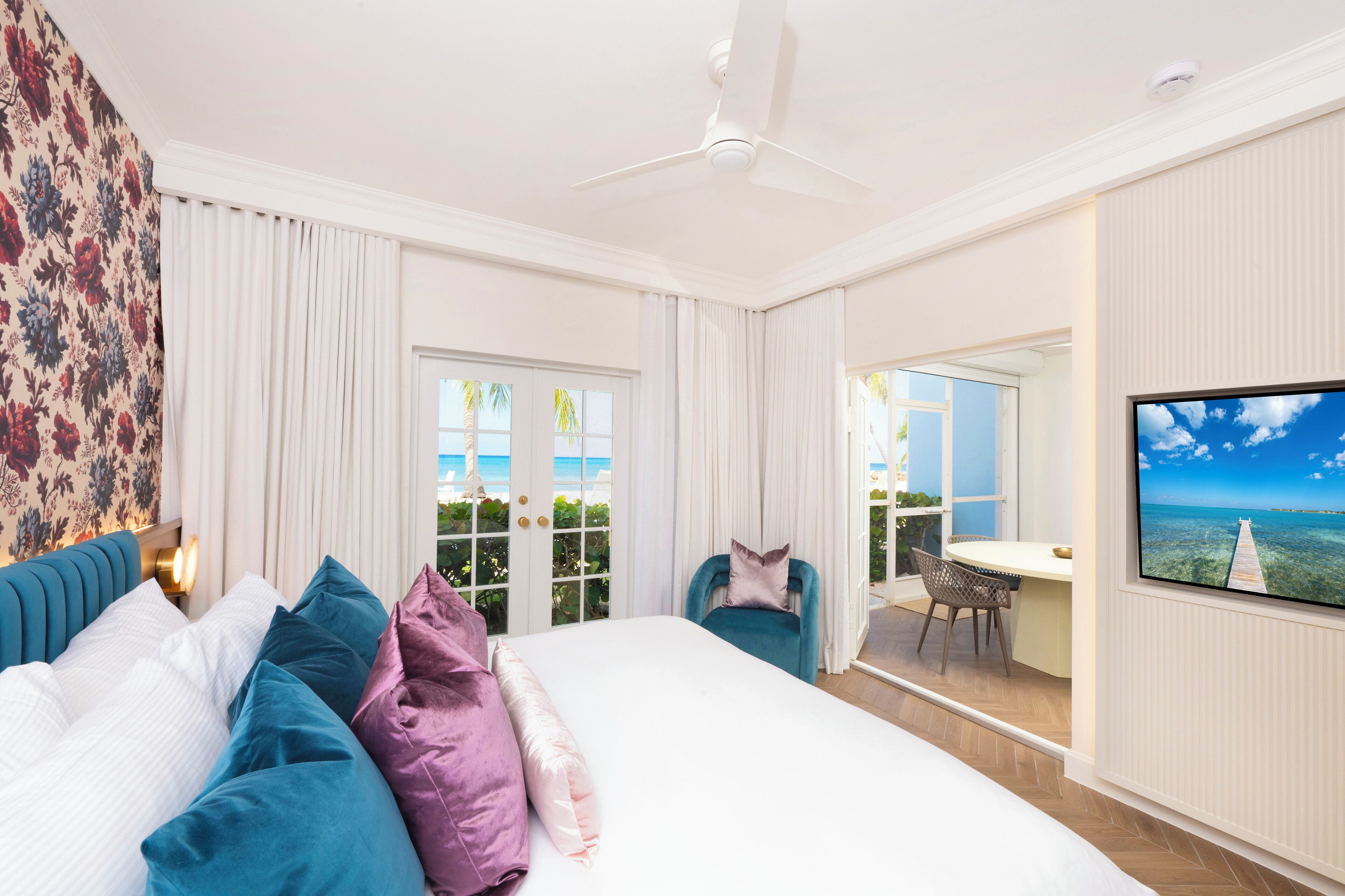 Quarto com cama, almofadas, ventilador de teto, TV e varanda com vista.