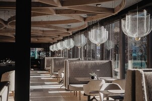 Um restaurante moderno com tetos altos, assentos estampados e luminárias pendentes.