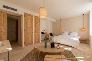 Quarto moderno com uma cama grande, portas de madeira, uma mesa de centro redonda com uma planta e duas luminárias pendentes.